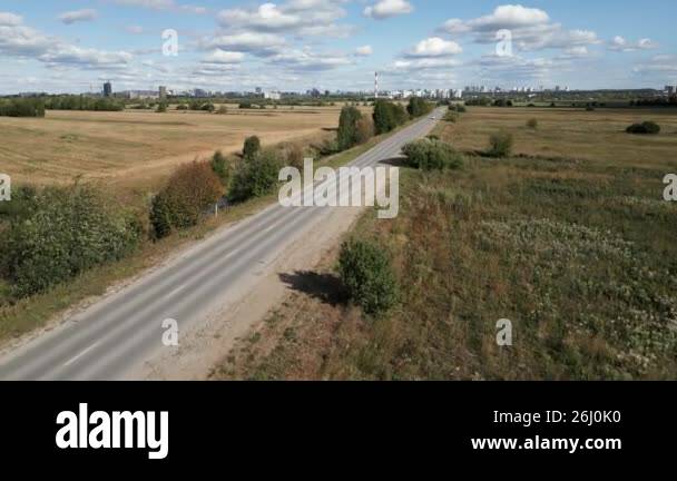 A tranquil road winds through lush fields with a stunning city skyline visible beneath a bright ...