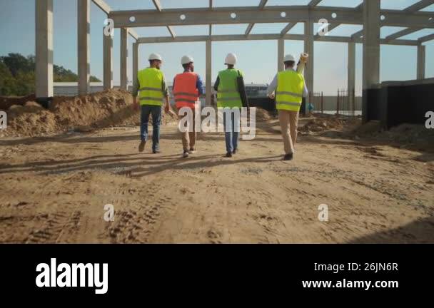 Back footage of group of builders in work clothes walking around ...
