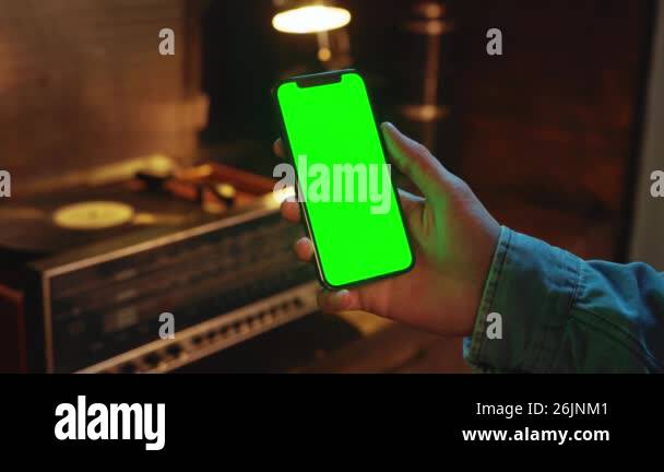 Shot of hands man using scrolling mobile phone with a vertical green screen indoors. Social ...