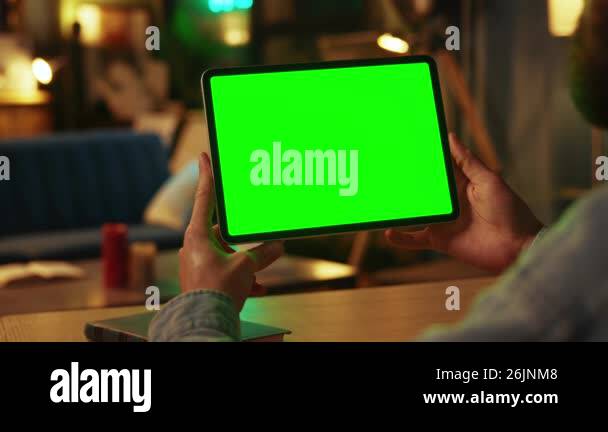 In dark room hands man holding scrolling and tapping on tablet computer ...