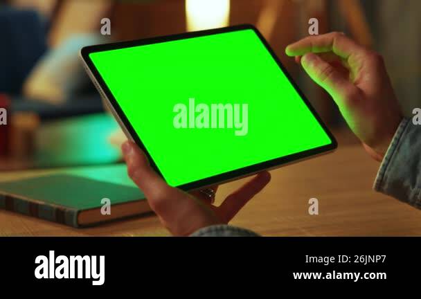 Young man holding scrolling and tapping on tablet computer with horizontal green screen. Mock up ...