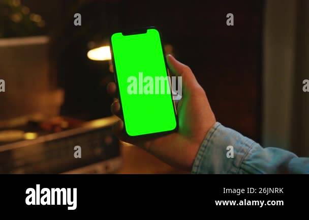 Close up mock up phone with vertical green screen. Hands using typing on a smartphone indoors ...