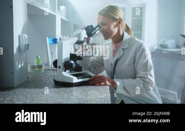 Smiling scientist woman looking under the microscope worker in the ...