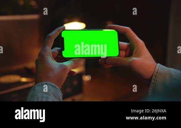 Close up hands using typing on a mobile phone with a horizontal green screen indoors. Social ...