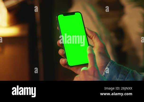 Shot of hands using typing on mobile phone with a vertical green screen indoors. Social media ...