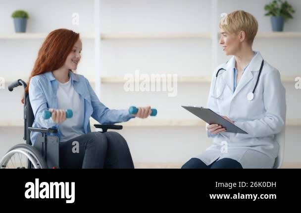 A redheaded teenager in a wheelchair lifts small weights during a ...