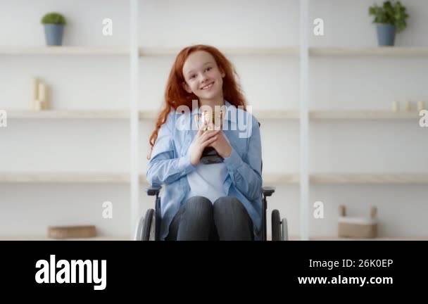A cheerful redhead girl with a disability is seated in her wheelchair ...