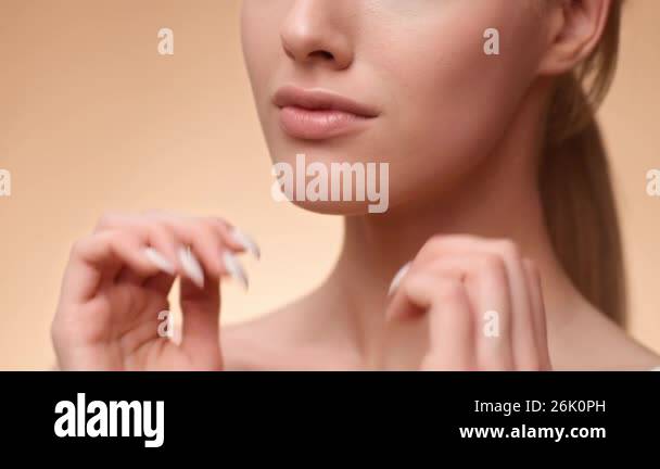 A young woman gently touches her face with both hands while applying ...