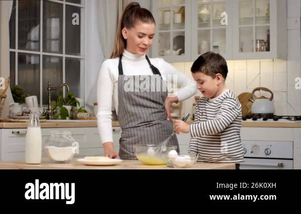 A woman and her son joyfully prepare to bake in a cozy kitchen, mixing ...