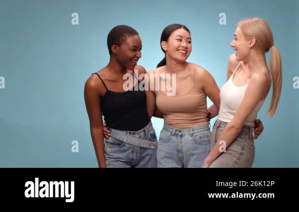 Three young women stand close together, laughing joyfully. They wear ...