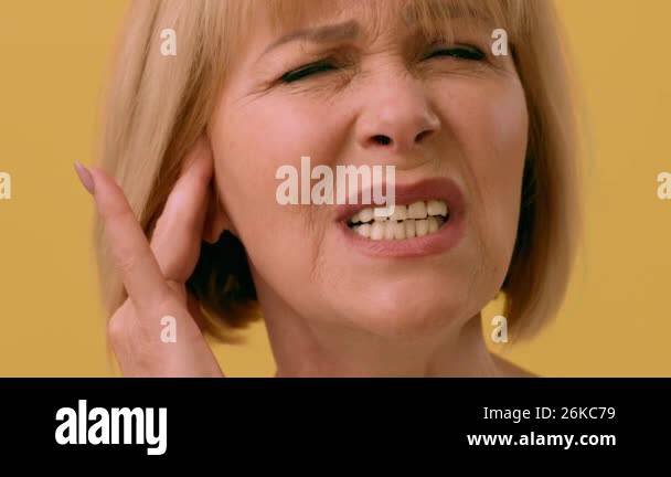A woman is grimacing while holding her ear, suggesting discomfort or ...