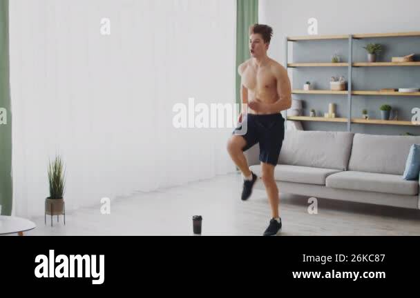 A fit young man engages in a workout routine at home, demonstrating an ...