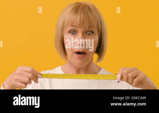 A woman focuses intently on measuring an object, using a yellow tape ...