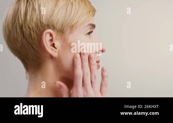 A Caucasian woman in her 50s is applying skincare products on her face ...