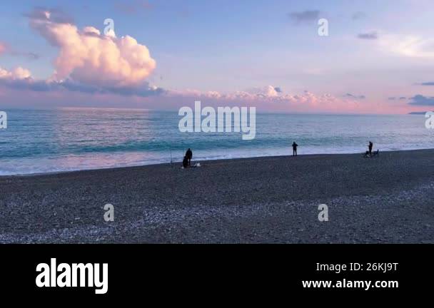 Several people enjoy fishing along the pebble beach as the sun sets ...