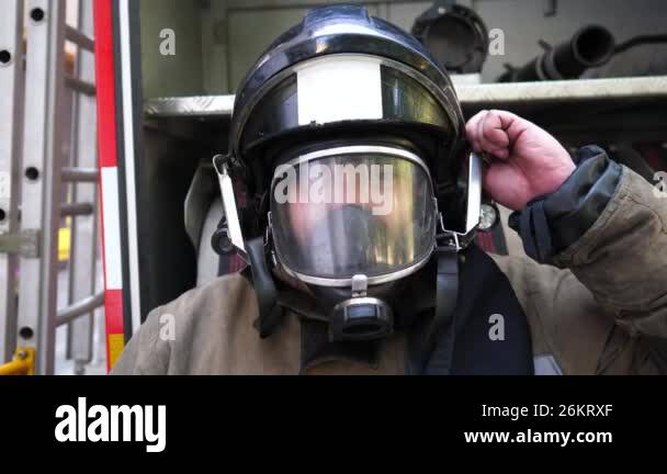 Male firefighter taking off oxygen mask near fire engine. Young fireman ...