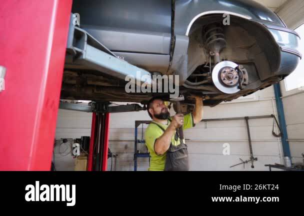 Adult male repairer works underneath a lifting vehicle at garage ...