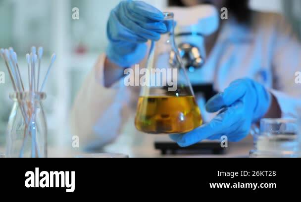 Laboratory technician conducts experiments with yellow liquids in glass ...