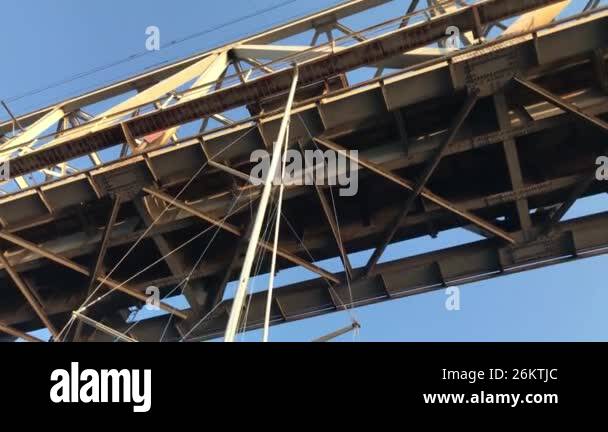 The mast of a yacht passes under a bridge. A freight train moves over a ...