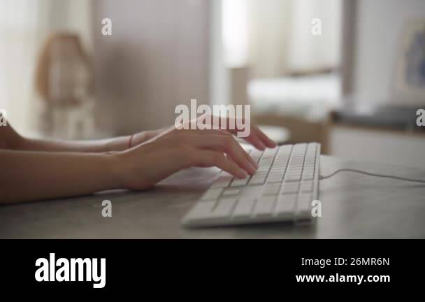 Closeup of hands typing on a wired keyboard in a softly lit home ...