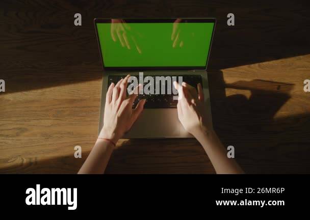 Overhead view of hands typing on a laptop with a green screen, placed ...