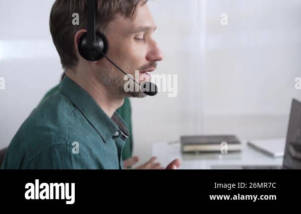 Focused male call center operator in green casual shirt is assisting clients online, providing ...