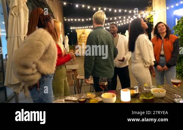 Multiracial friends saying goodbye after a dinner on a terrace at night ...