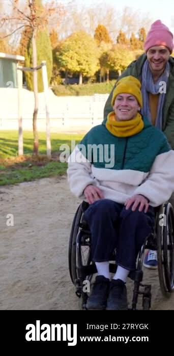 Supportive friend propelling wheelchair using companion through sunlit ...