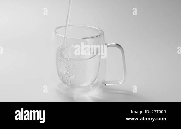 A stream of clean water flows into a glass cup on a white background. A ...
