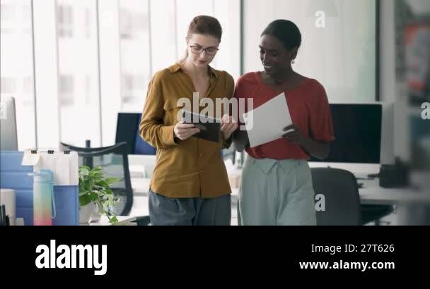 Two attractive multiethnic women colleagues engage in teamwork standing ...