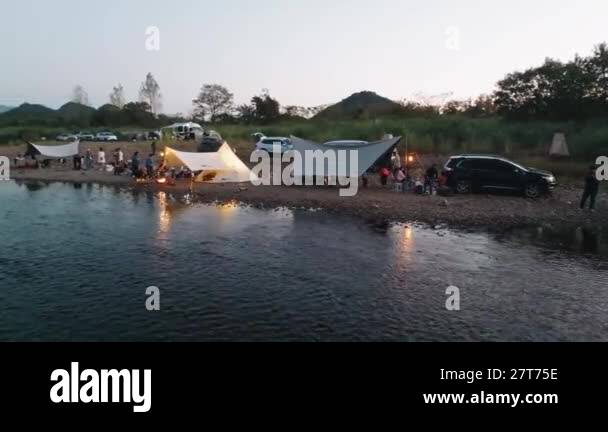 Campers enjoy an evening gathering around a fire near the riverbank ...