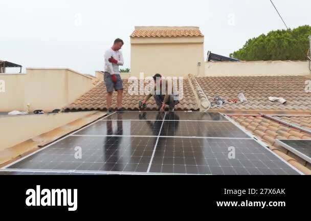 Two technicians working on securing solar panels on a red-tiled roof ...