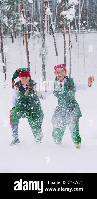 Two elves in green suits with hats are playing and throwing up snow ...