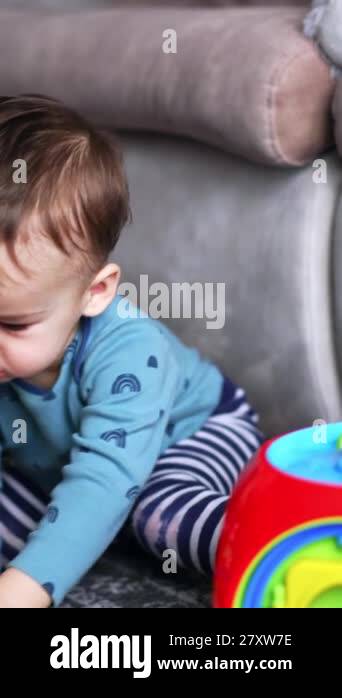Dark-haired Caucasian toddler boy sitting on the floor next to the sofa ...