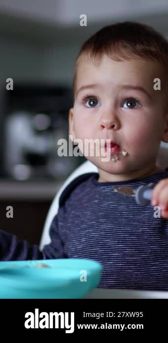 Caucasian toddler sitting at high chair chewing food thoroughly. Baby ...