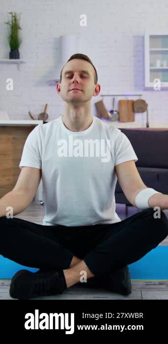 Young man sitting in yoga pose in the kitchen. Guy in white t-shirt ...