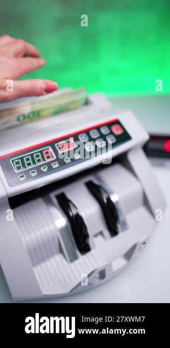 A large stack of one hundred euro bills is placed into the slot of cash ...