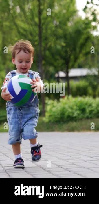 Excited Caucasian toddler runs carrying the ball. Baby boy on the walk ...