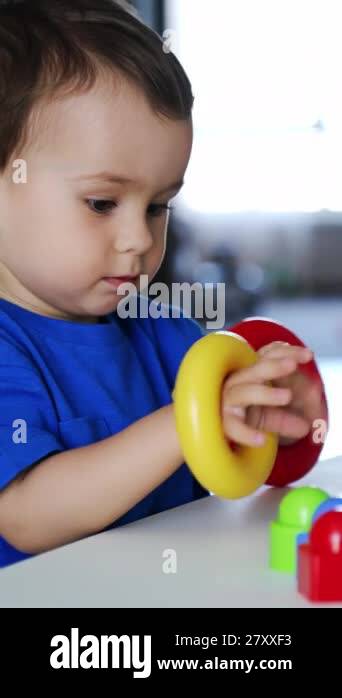 Charming cute Caucasian baby boy sits at the desk playing with pyramid ...