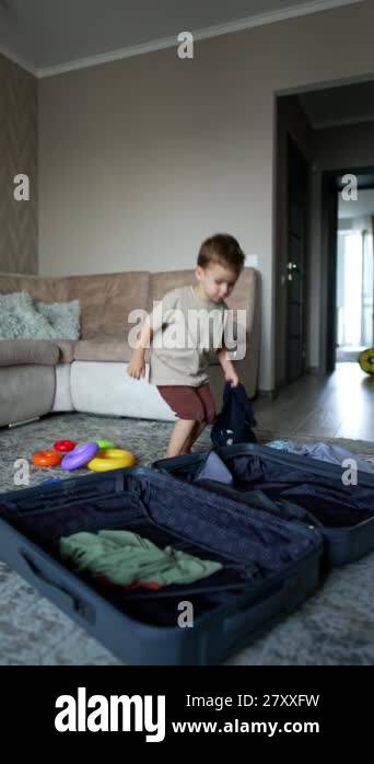 Little baby boy packs a big grey suitcase lies opened on the floor ...