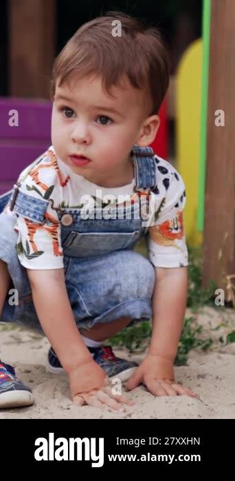 Caucasian toddler playing in the sand at the playground. Calm boy looks ...