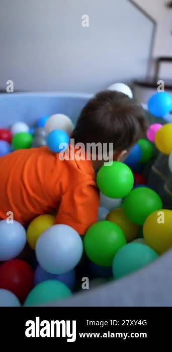 Energetic baby boy tumbling in the colorful balls in the dry pool ...