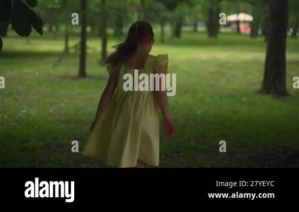 Girl with Down syndrome in yellow dress runs freely across grassy park ...