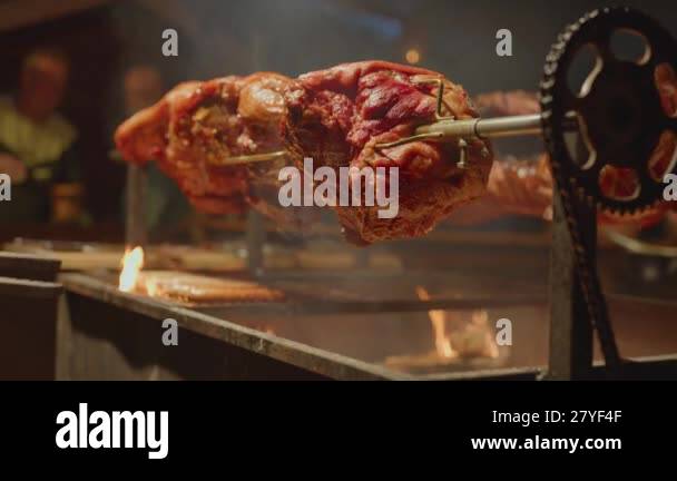 A large piece of meat is being cooked on a spit. The meat is being ...