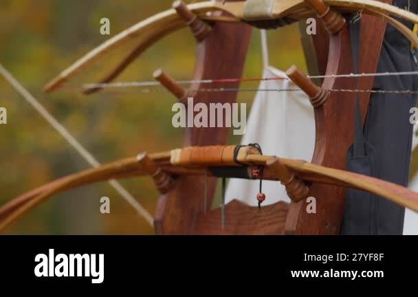 A wooden bow is hanging on a rack with other bows. The bow is brown and ...