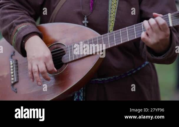 A woman is playing a guitar. The guitar is an old fashioned instrument ...