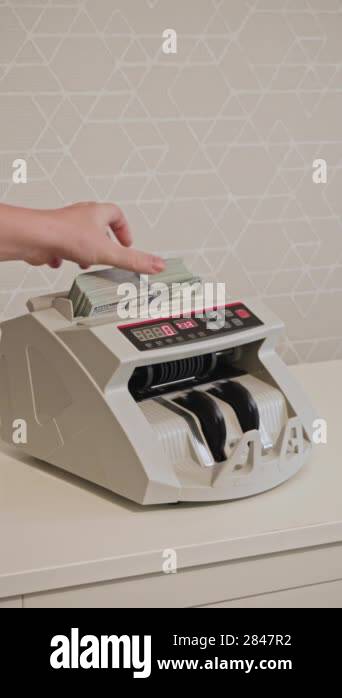 A person is using a bill counting machine to sort and count stacks of ...