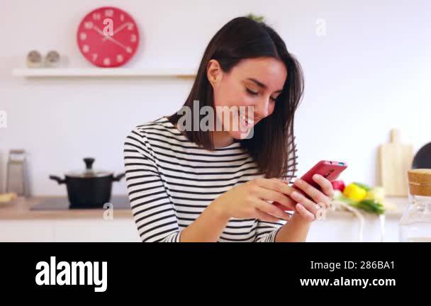 Young happy woman using mobile phone in the kitchen at home, having fun ...