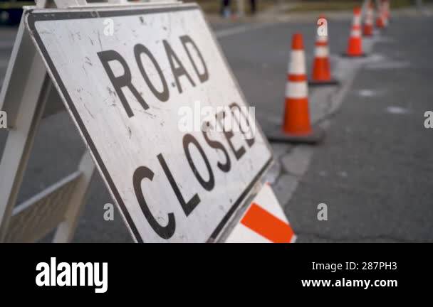 A close-up view of a "Road Closed" sign with traffic cones lining the ...