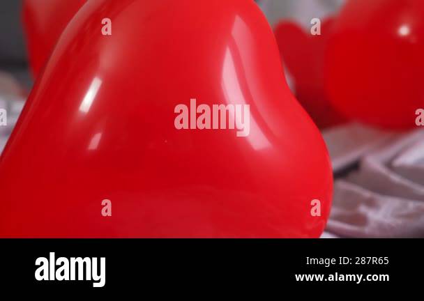 A red engagement ring box lies on a couch surrounded by heart-shaped ...